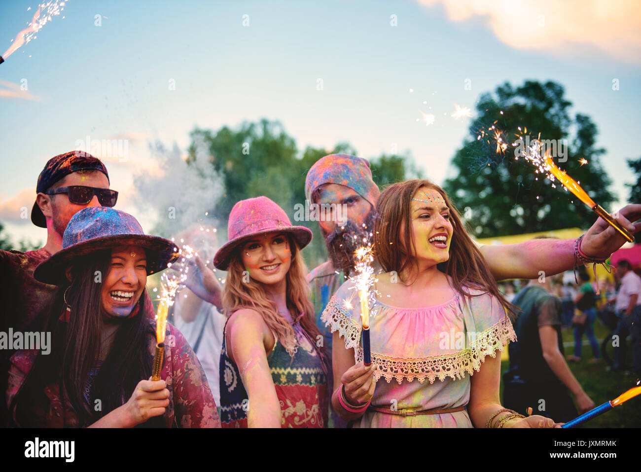 Young adults covered in coloured chalk powder dancing with sparklers at ...