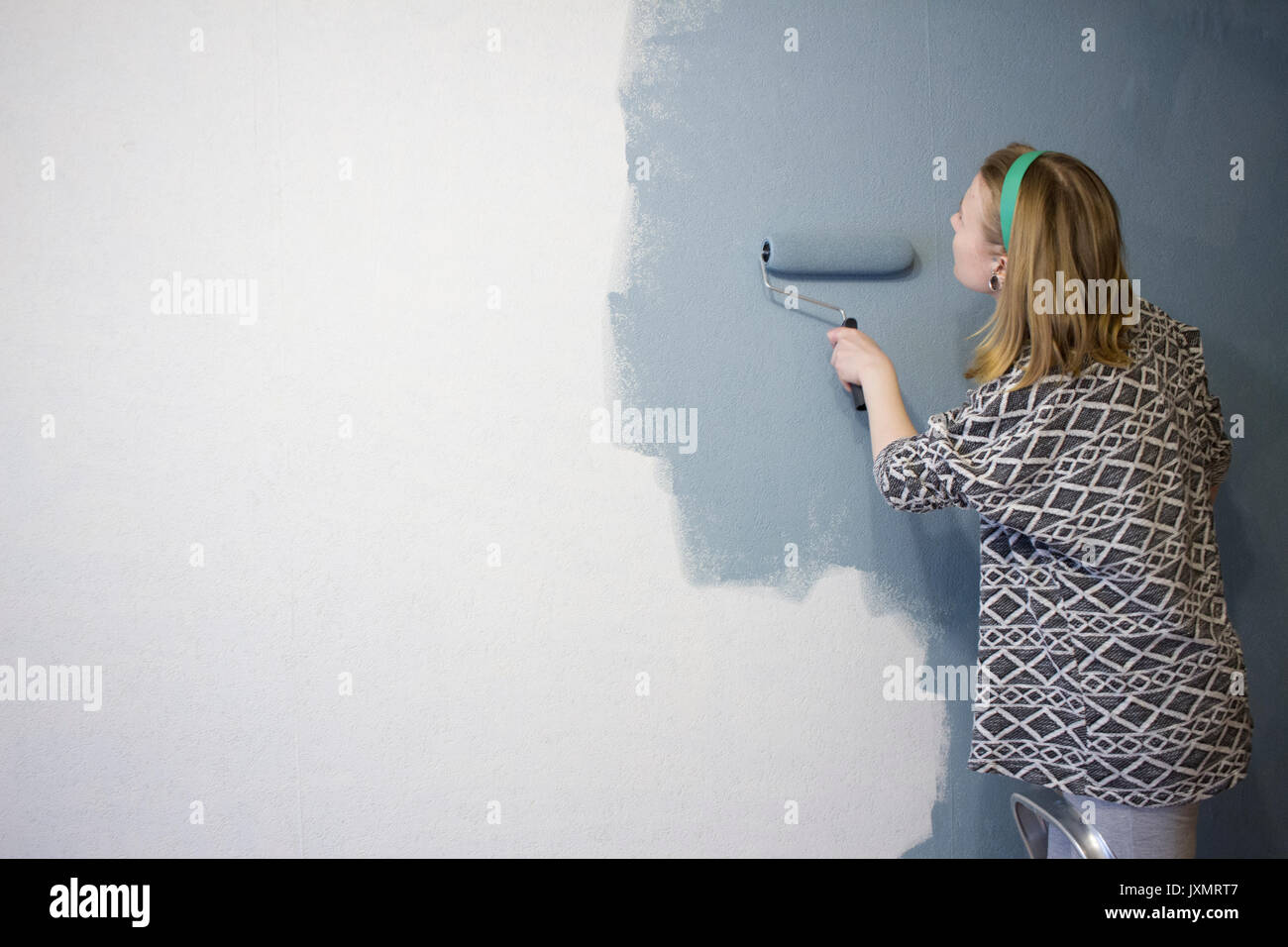 Young woman on step ladder applying grey paint to interior wall at home ...