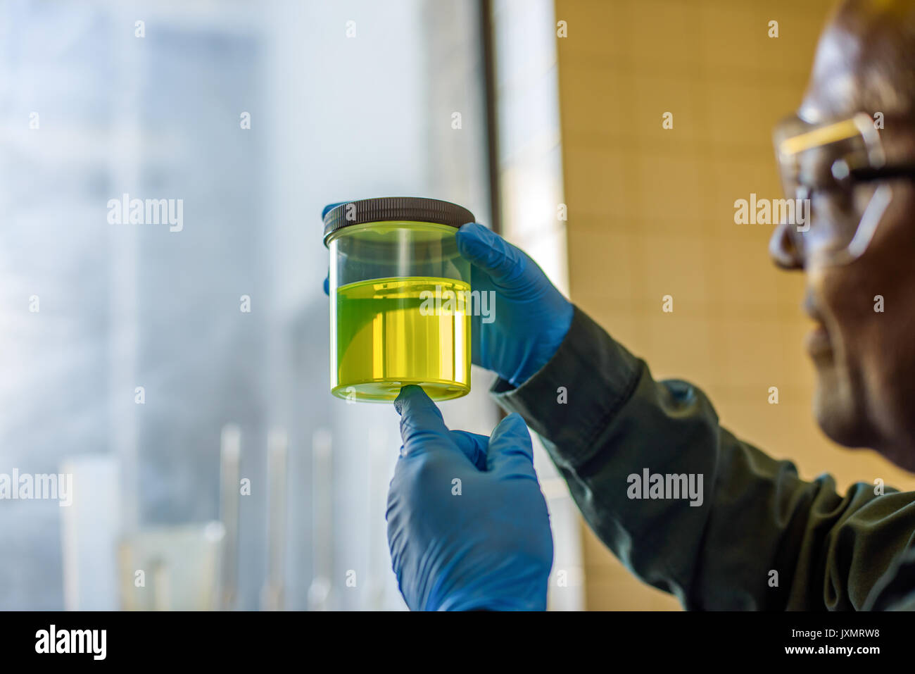 Lab technician inspecting beaker of yellow biofuel in biofuel plant ...