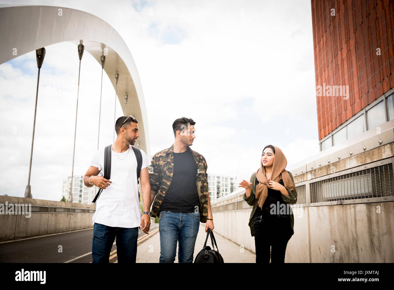 Three friends, walking across urban bridge Stock Photo - Alamy