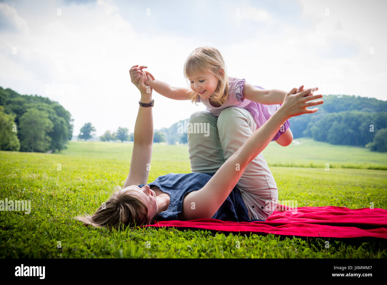 Mid adult woman lying on back balancing daughter in rural field Stock ...