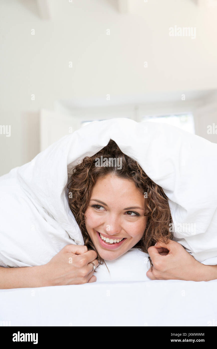 Woman lying on bed underneath quilt smiling Stock Photo - Alamy