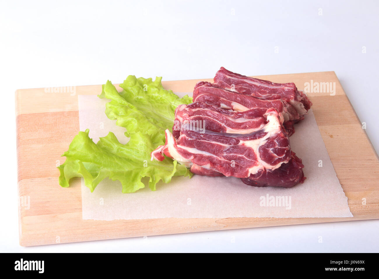 Raw beef edges and lettuce leaf on wooden desk isolated on white ...