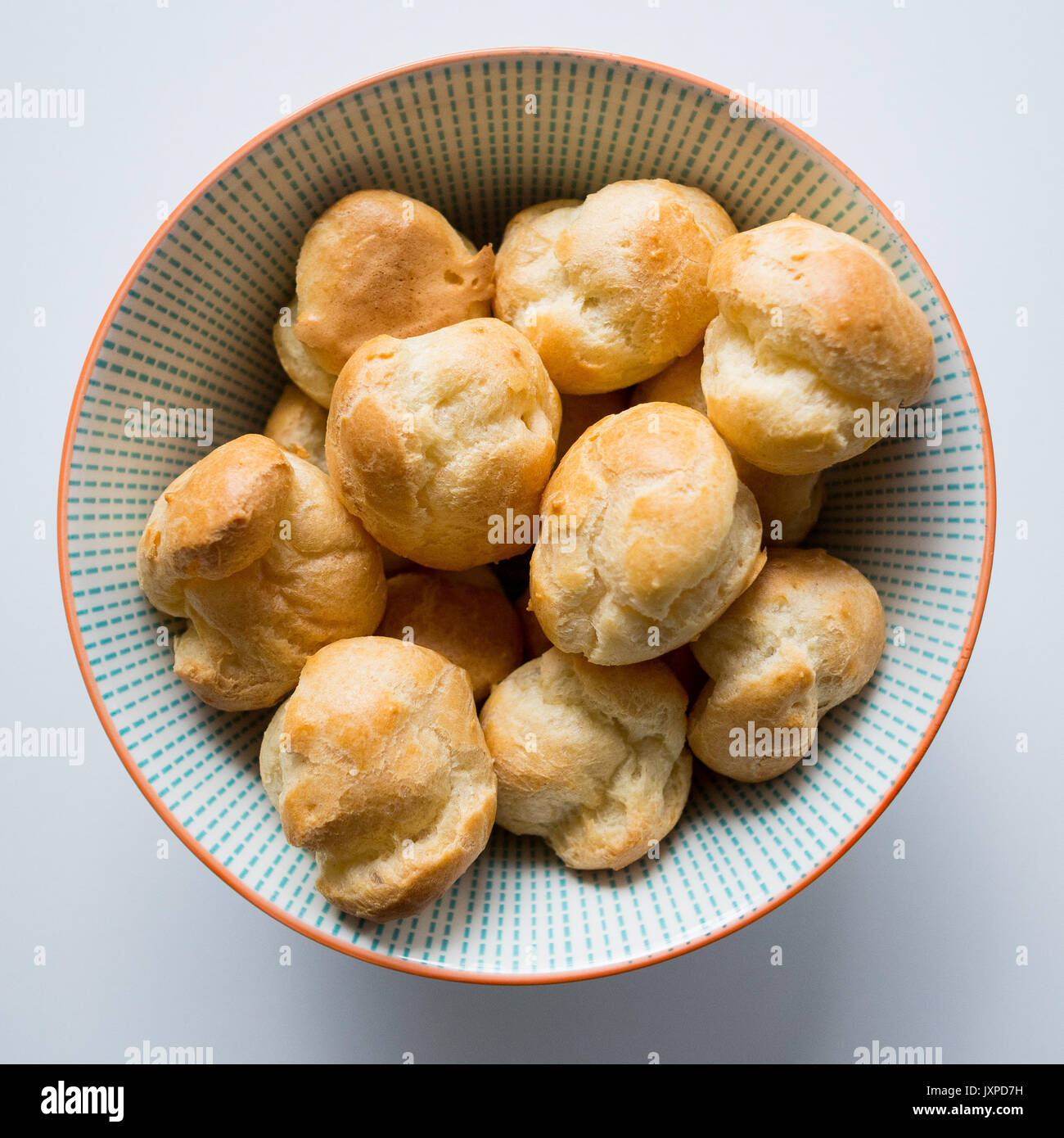 Top view of cream puffs in a blue dotted bowl on a white table. Squared ...
