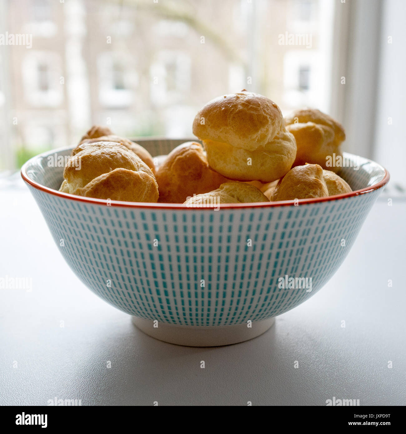 Side view of cream puffs in a blue dotted bowl on a white table ...