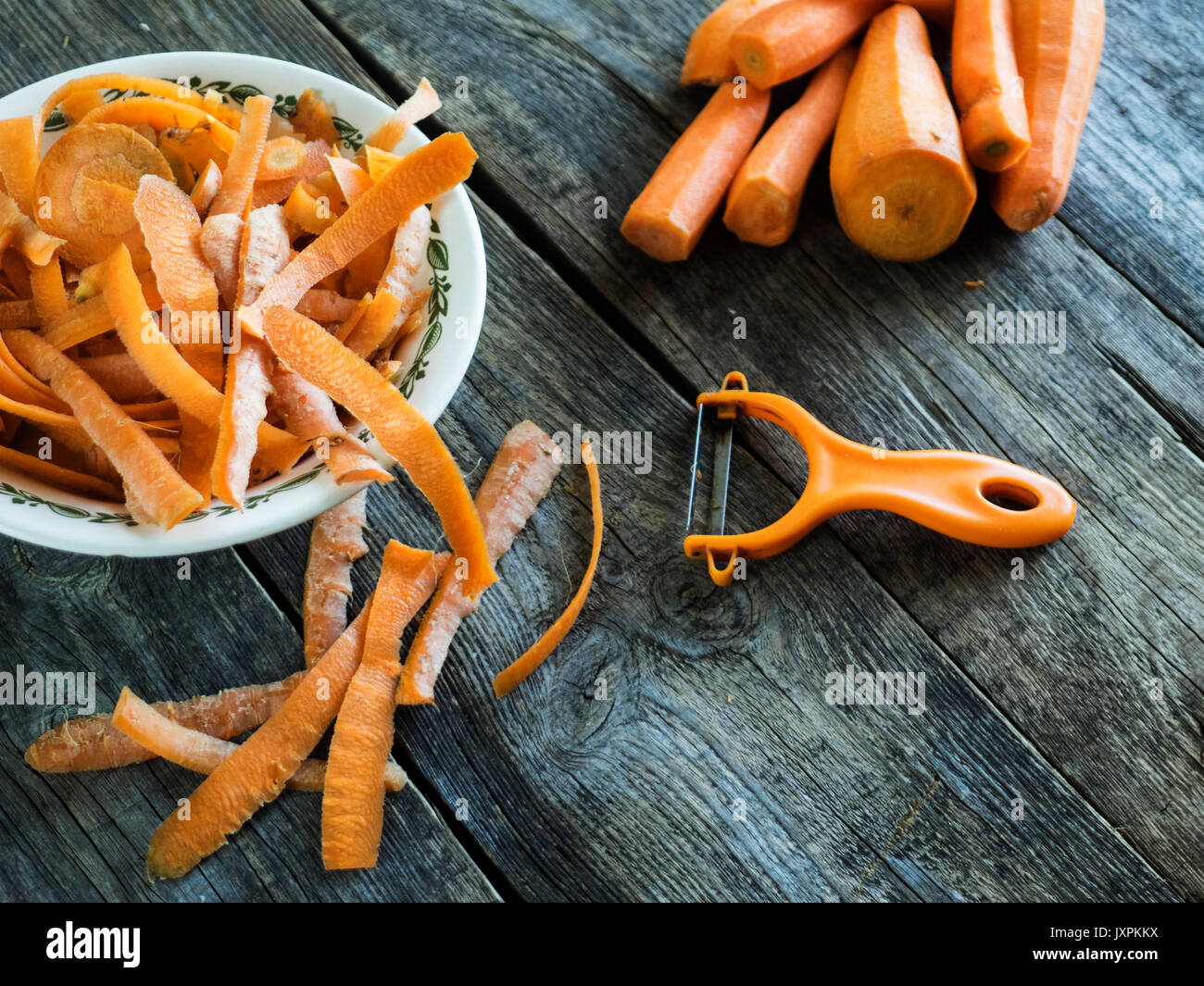 Carrots, carrot skin in a bowl and a peeler on an old weathered wooden ...