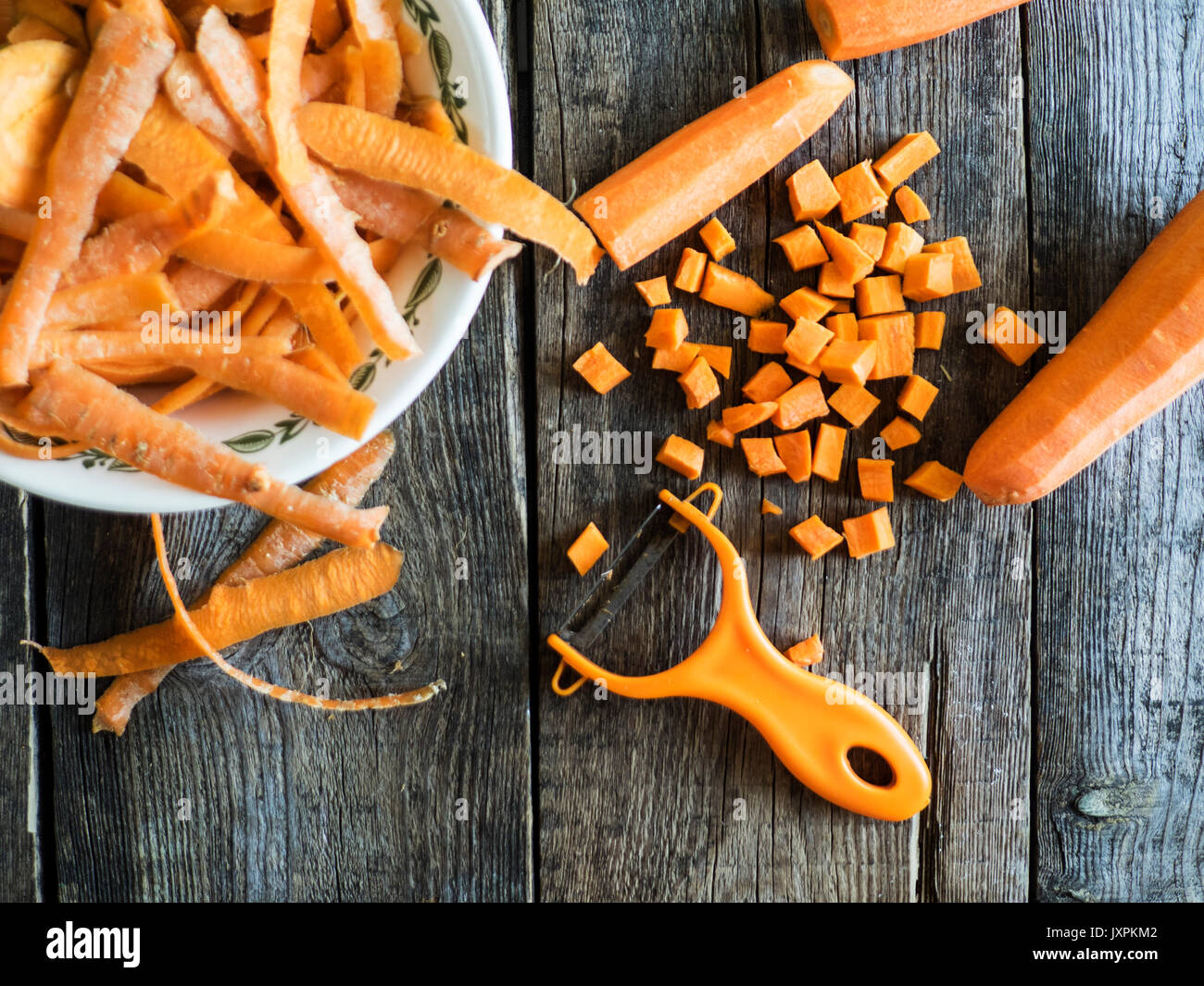 Carrots, carrot skin in a bowl and a peeler on an old weathered wooden ...