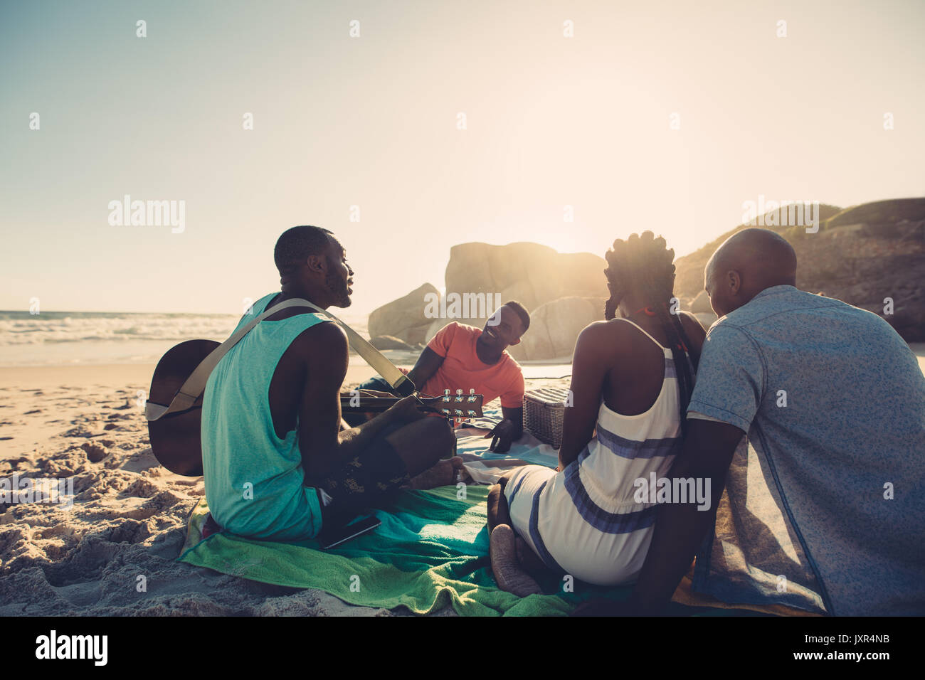African young man singing and playing guitar on the beach. Group of ...