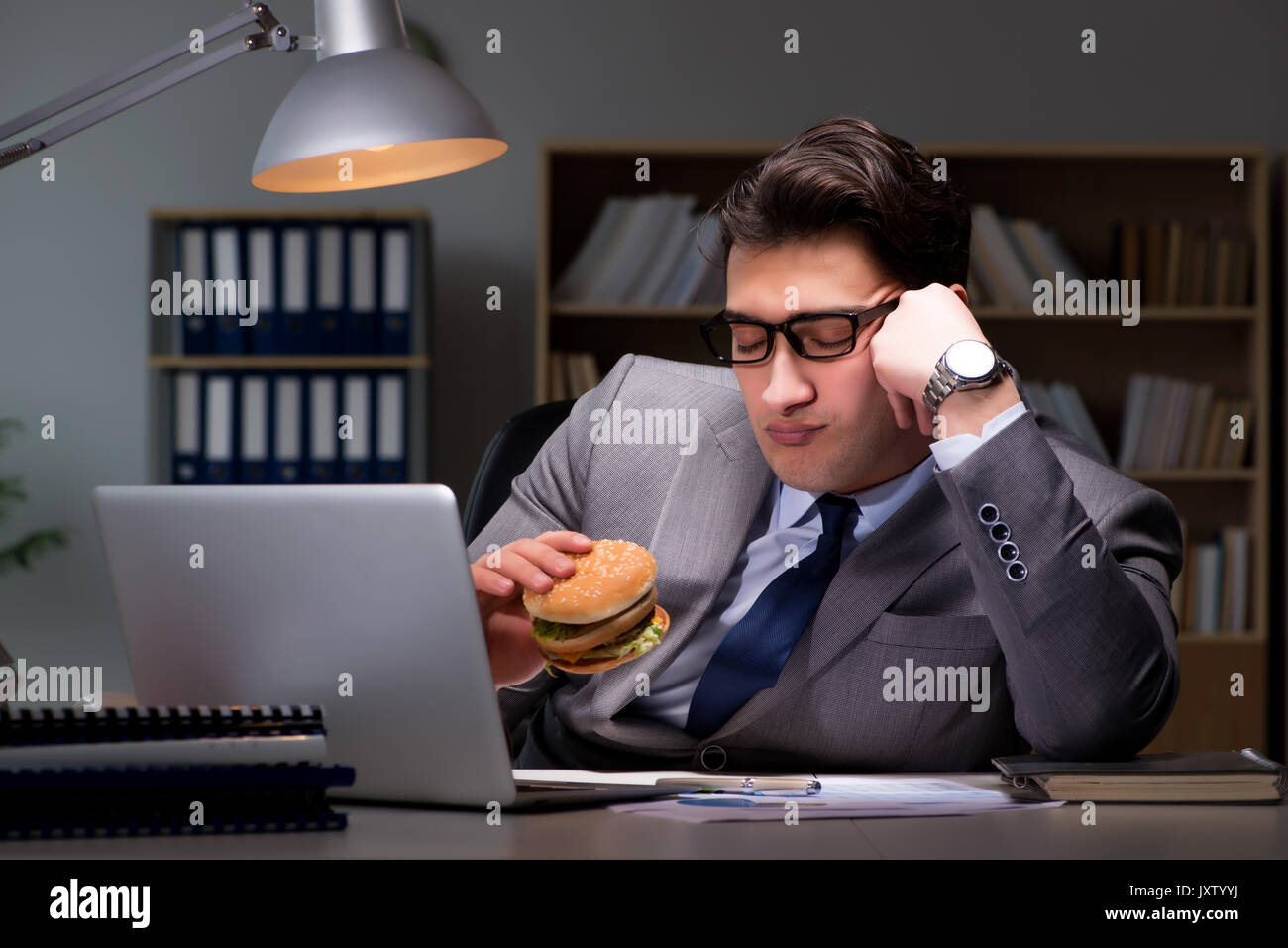 Businessman late at night eating a burger Stock Photo - Alamy