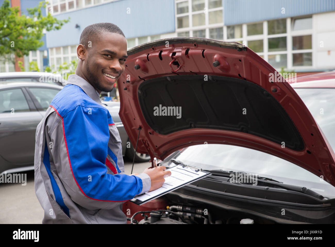 Young African Mechanic Writing On Clipboard In Front Of Open Car Engine ...