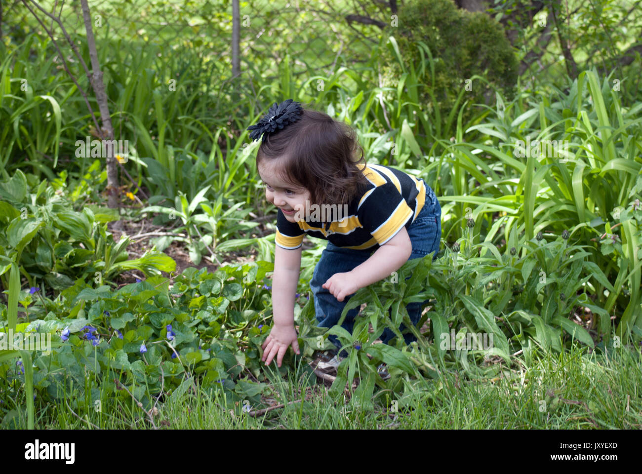 Young brunette girl looks out as she reaches down to touch the ground ...