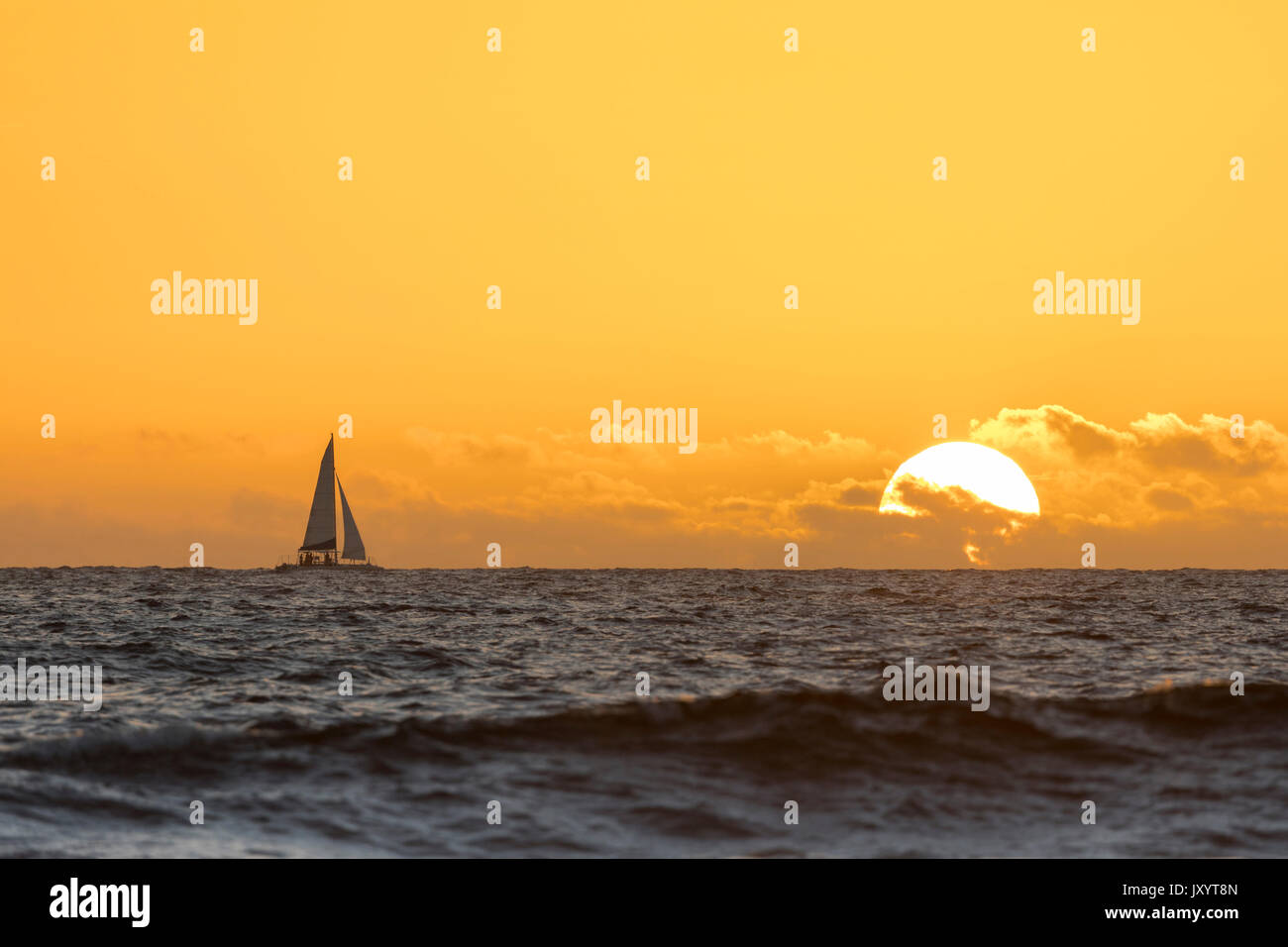 Distant sailboat in ocean at sunset Stock Photo - Alamy