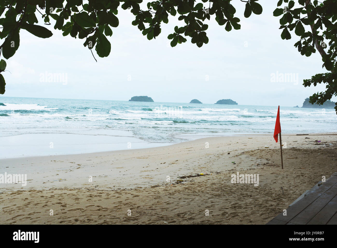Seascape and red flag on beach with leaves.Beach and sea with wave in ...
