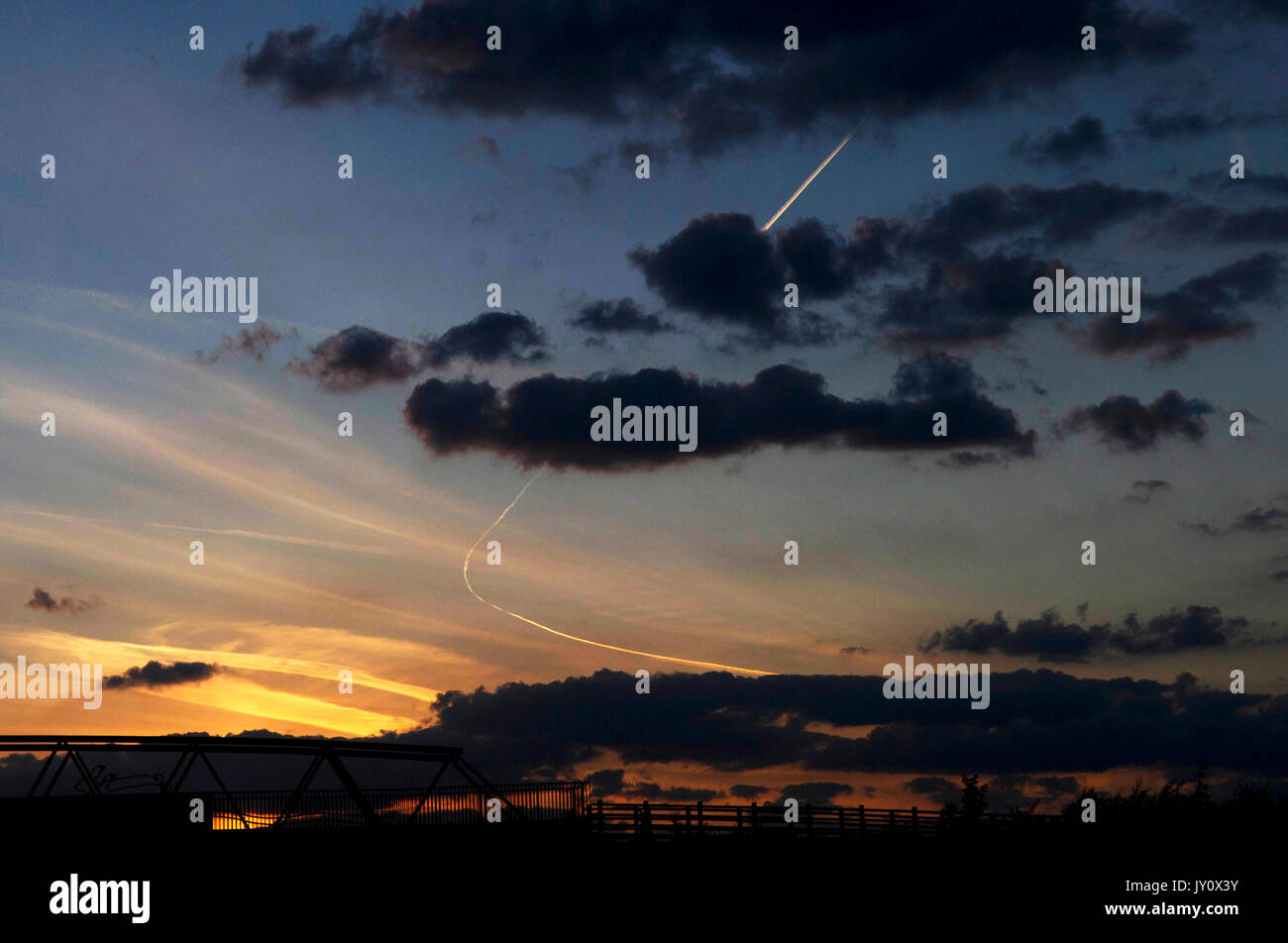 Aeroplane Contrails in the sky with black clouds and at sunset Stock ...