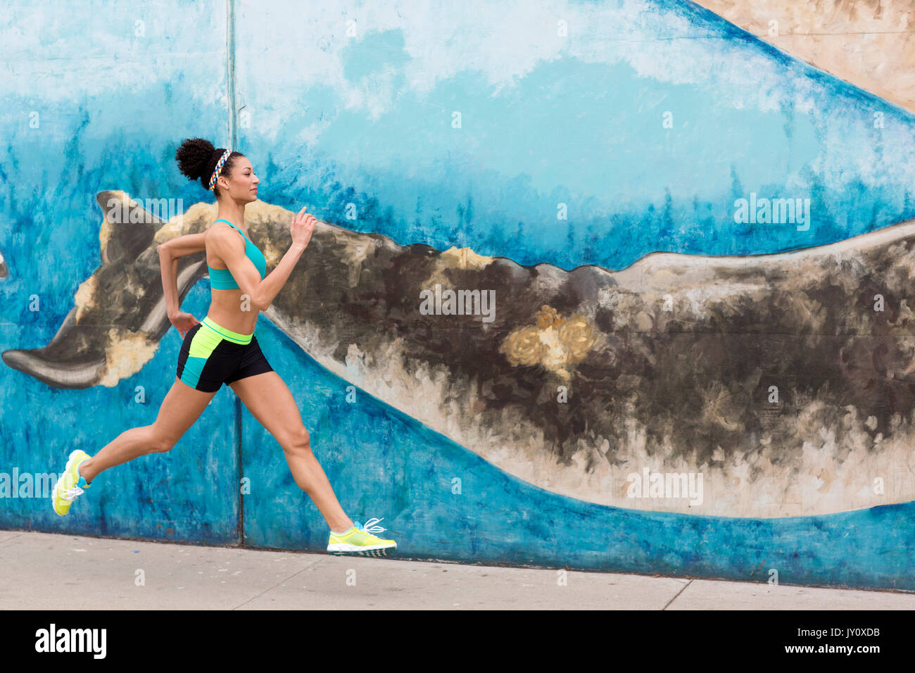 Mixed Race woman running on sidewalk near mural Stock Photo - Alamy