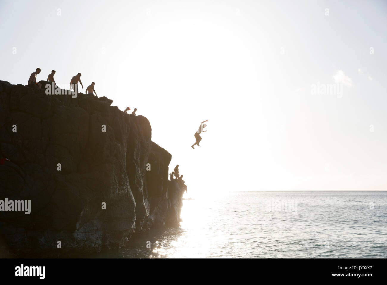 Friends jumping from cliff into ocean Stock Photo - Alamy