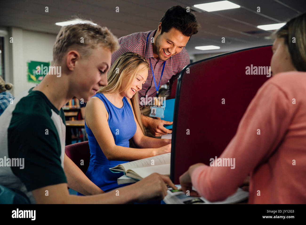 Students are working on computers with textbooks. A male teacher is ...