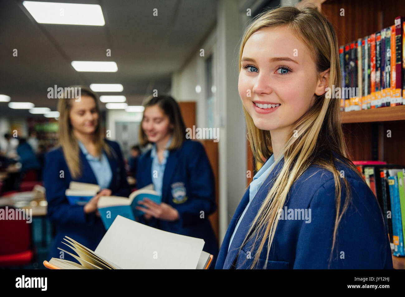 Teenage girl is standing in the library at school with a book in her ...