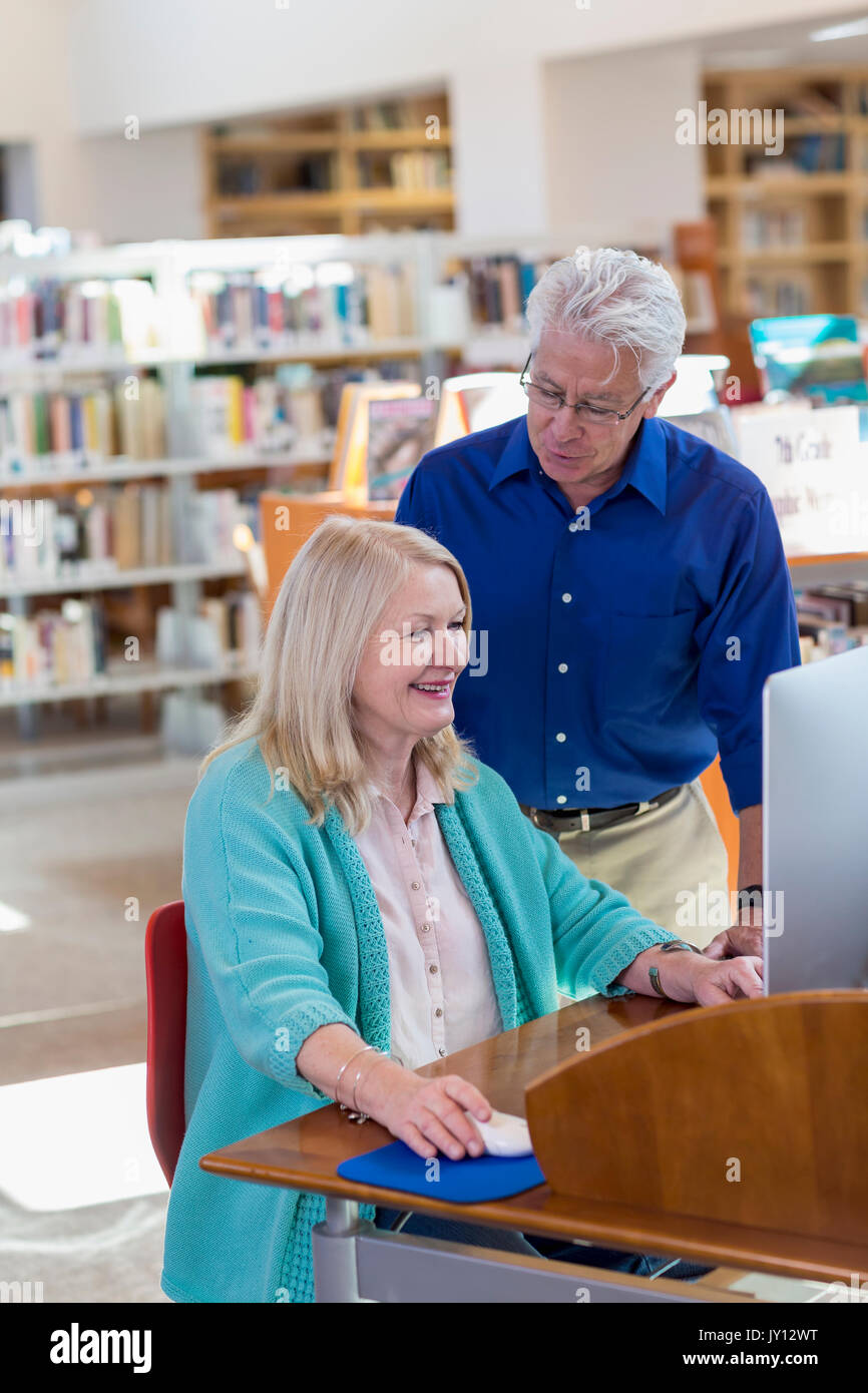 Older man watching woman using computer in library Stock Photo - Alamy