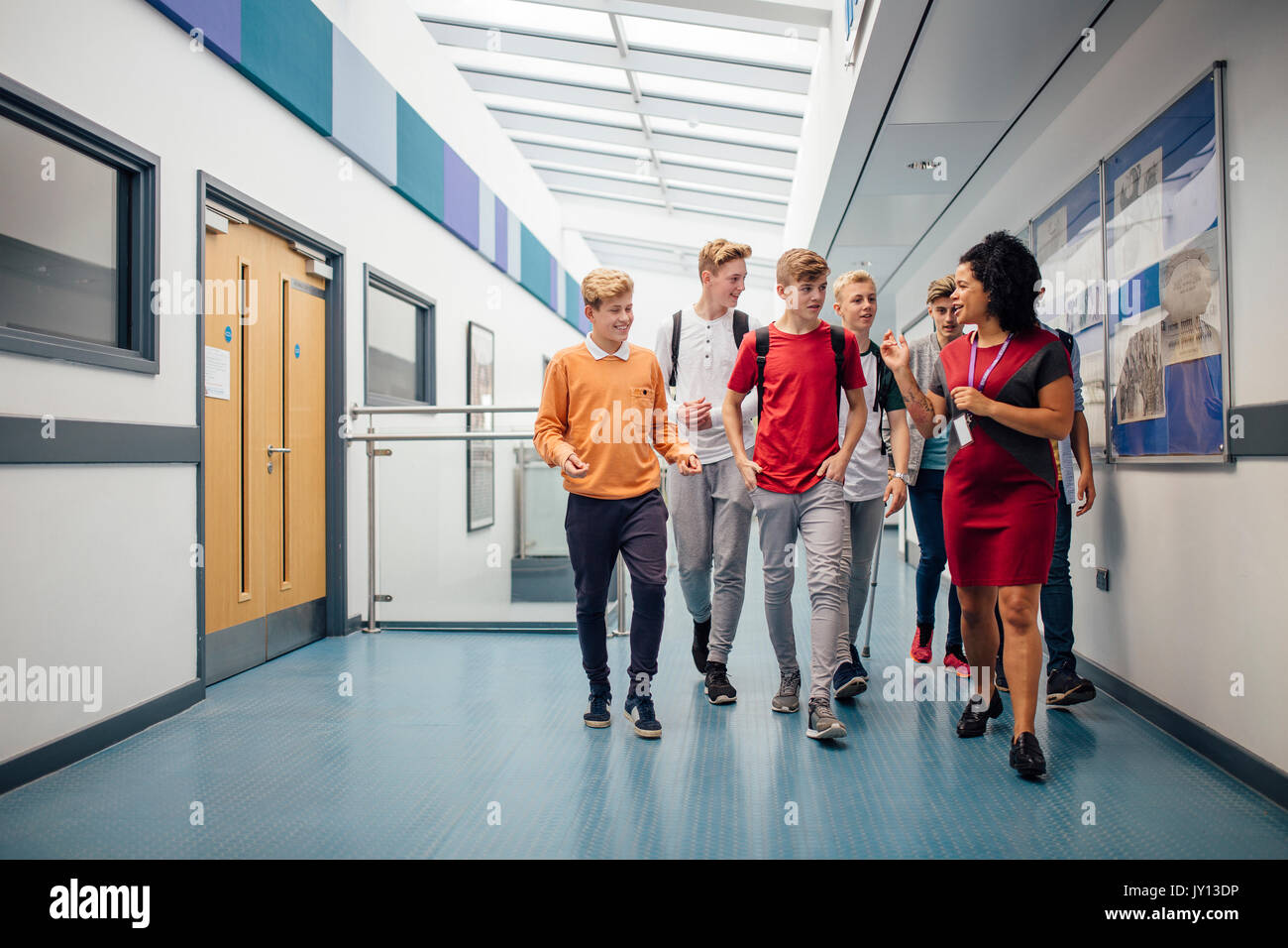 Female teacher is walking down the school hall with a group of male ...