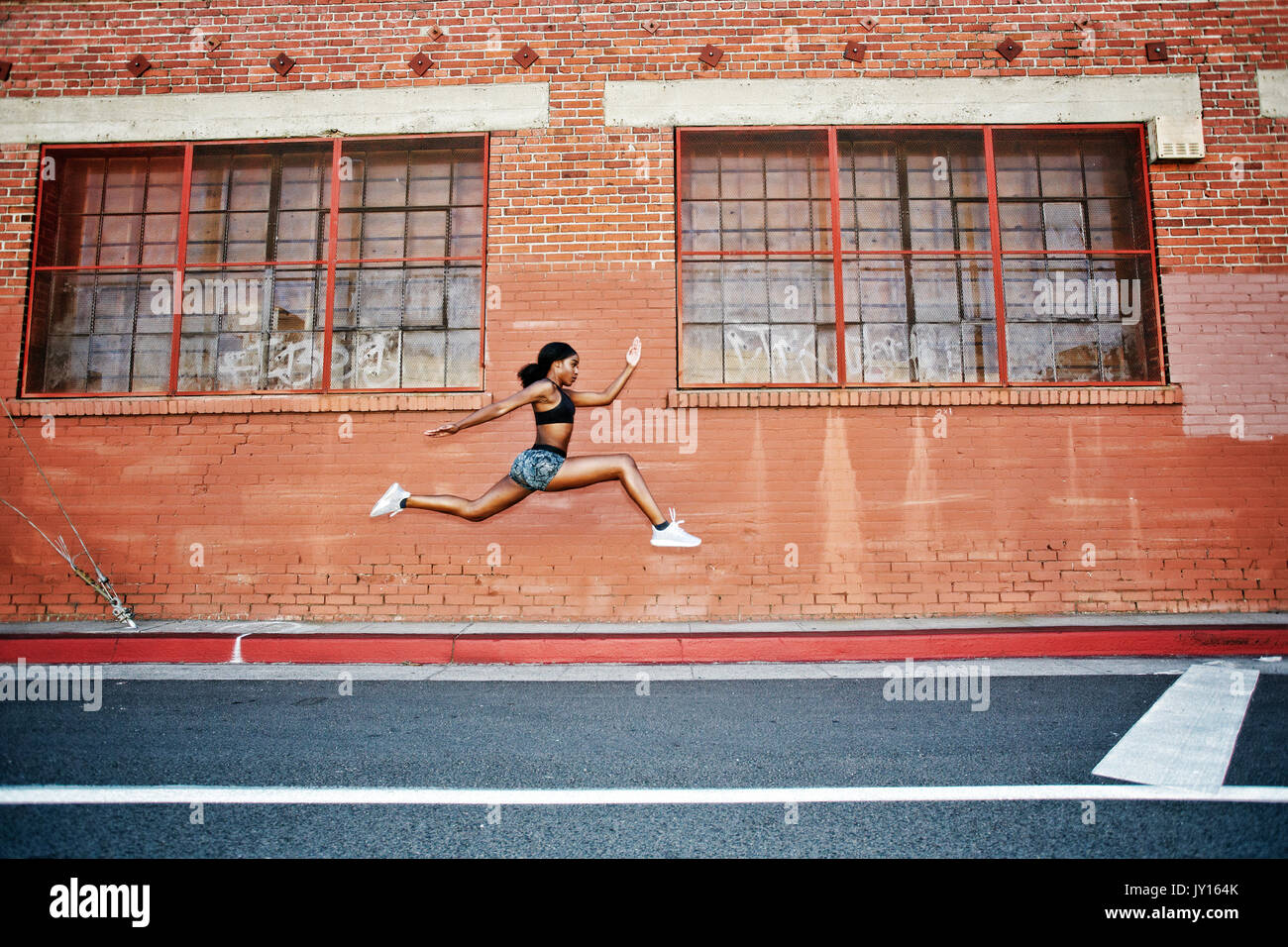 Mixed Race woman running and jumping near urban wall Stock Photo - Alamy