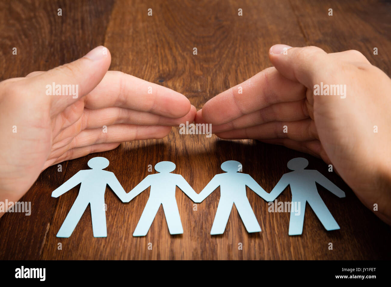 Close-up Of Person Hand Protecting Human Figure Cutout On Wooden Desk ...