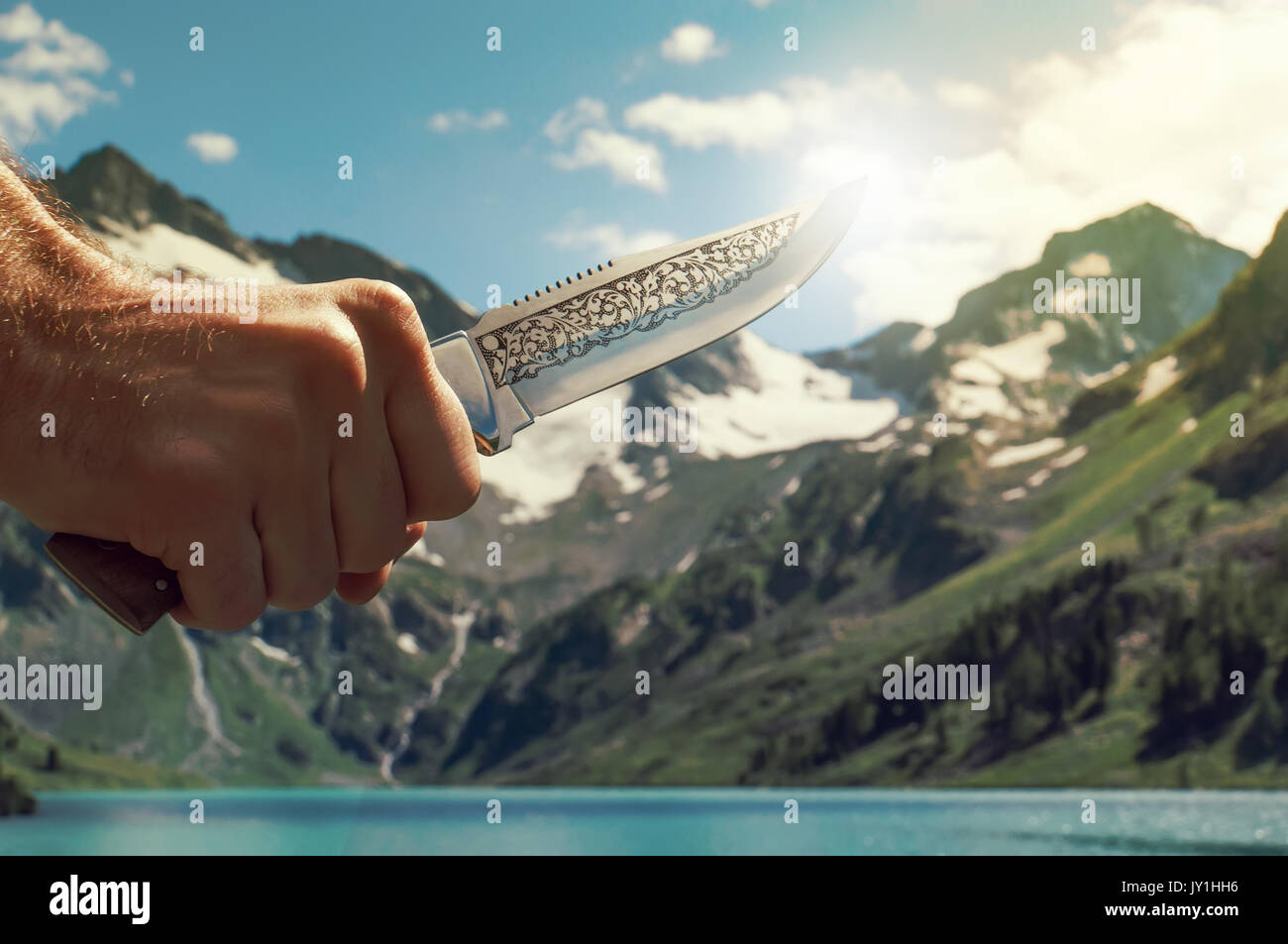 The hand holding the knife. Against the bright sun and mountain scenery ...