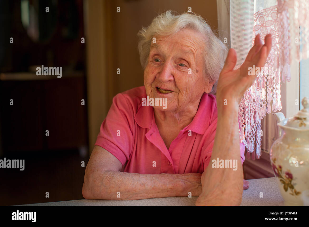 Elderly woman in red talking animatedly sitting at the table Stock ...