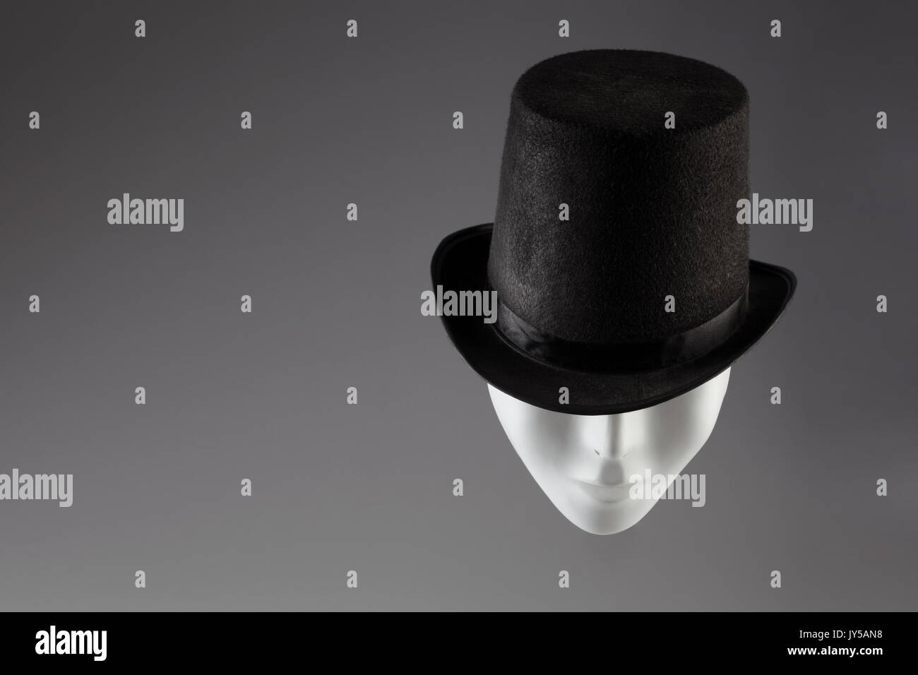 White mask hiding eyes under black top hat on grey background with copy ...