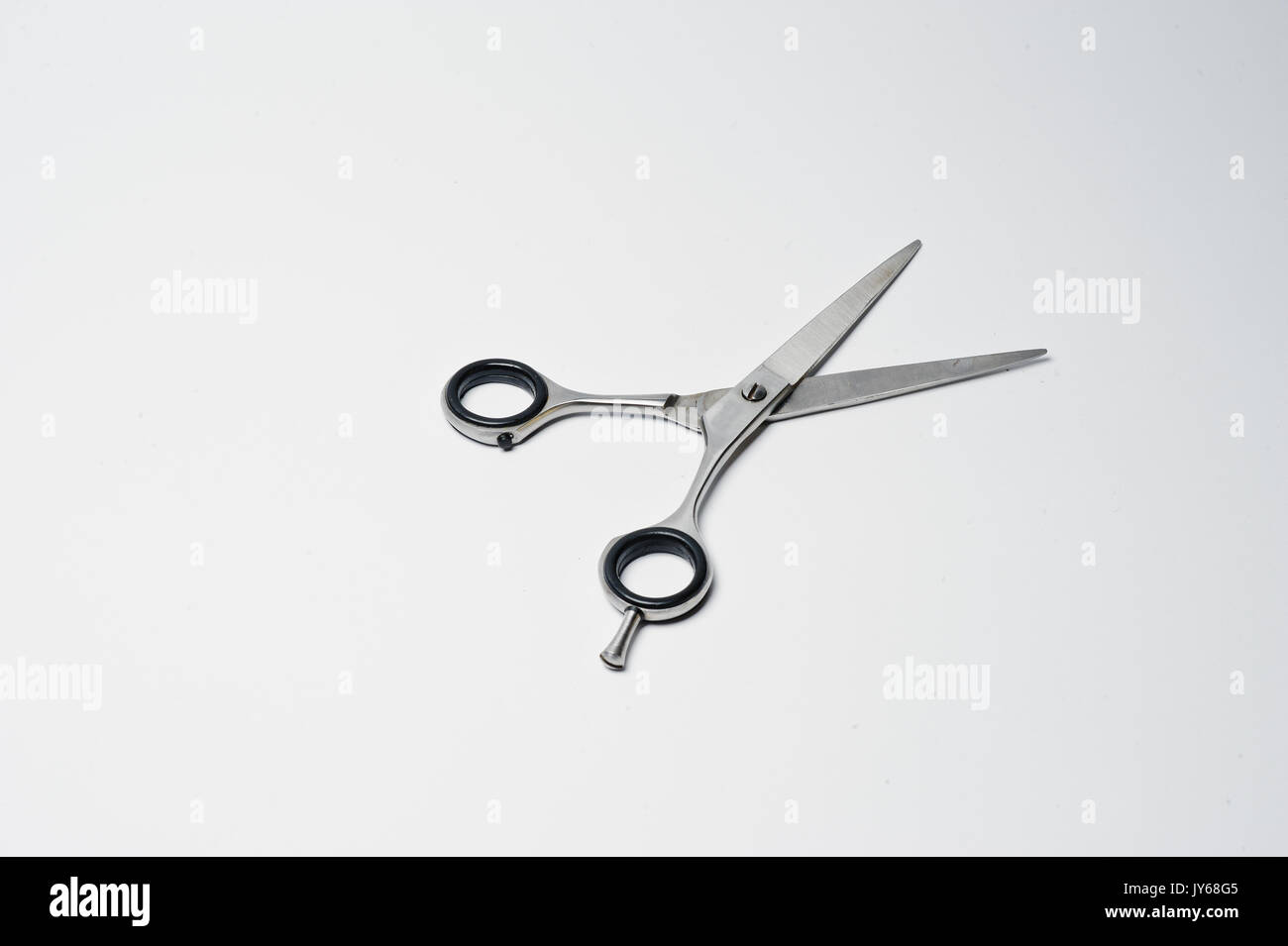 Close-up photo of a pair of silver scissors laying on the white surface ...