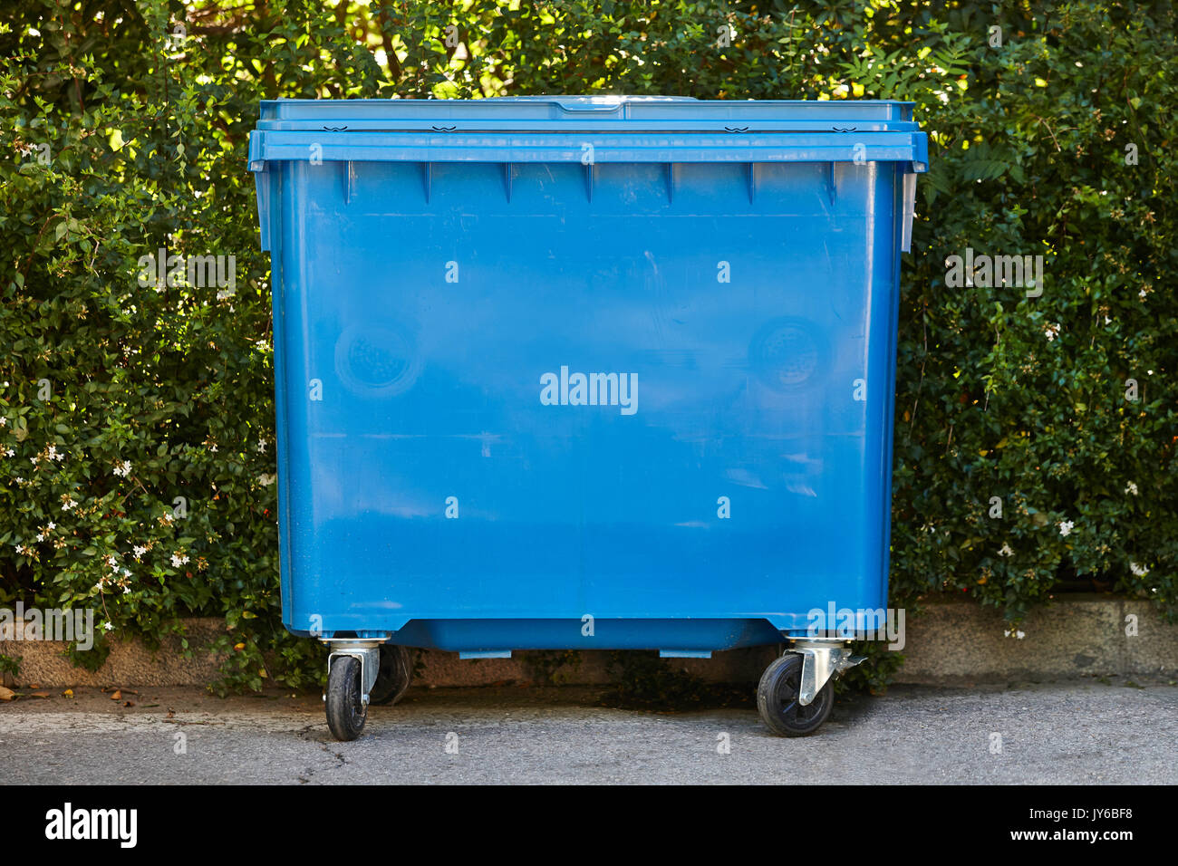 Blue recycling container for paper with green bush background ...