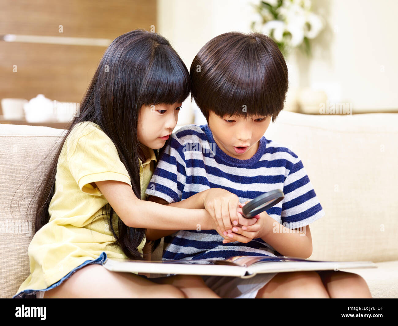 asian brother and sister sitting on sofa at home using a magnifying ...