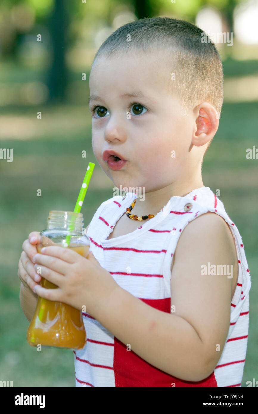 Portrait of a cute little boy outside while drinking juice from a glass ...