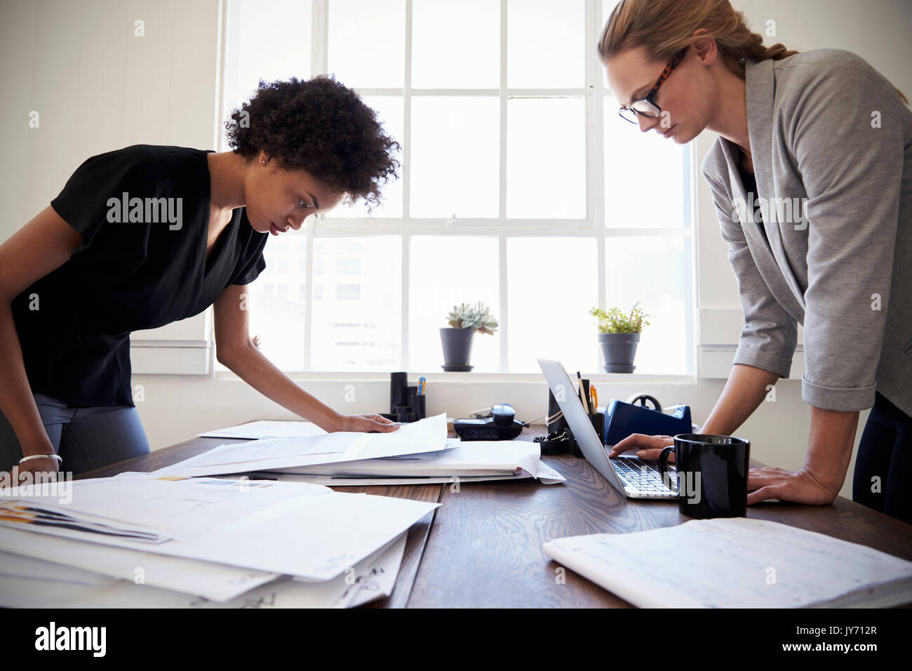 Two Women Work At Opposite Sides Of An Office Desk Close Up Stock