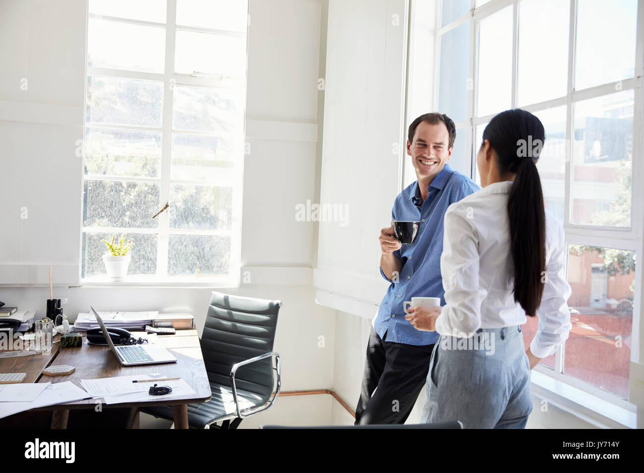 Two young business colleagues talk by window in an office Stock Photo ...