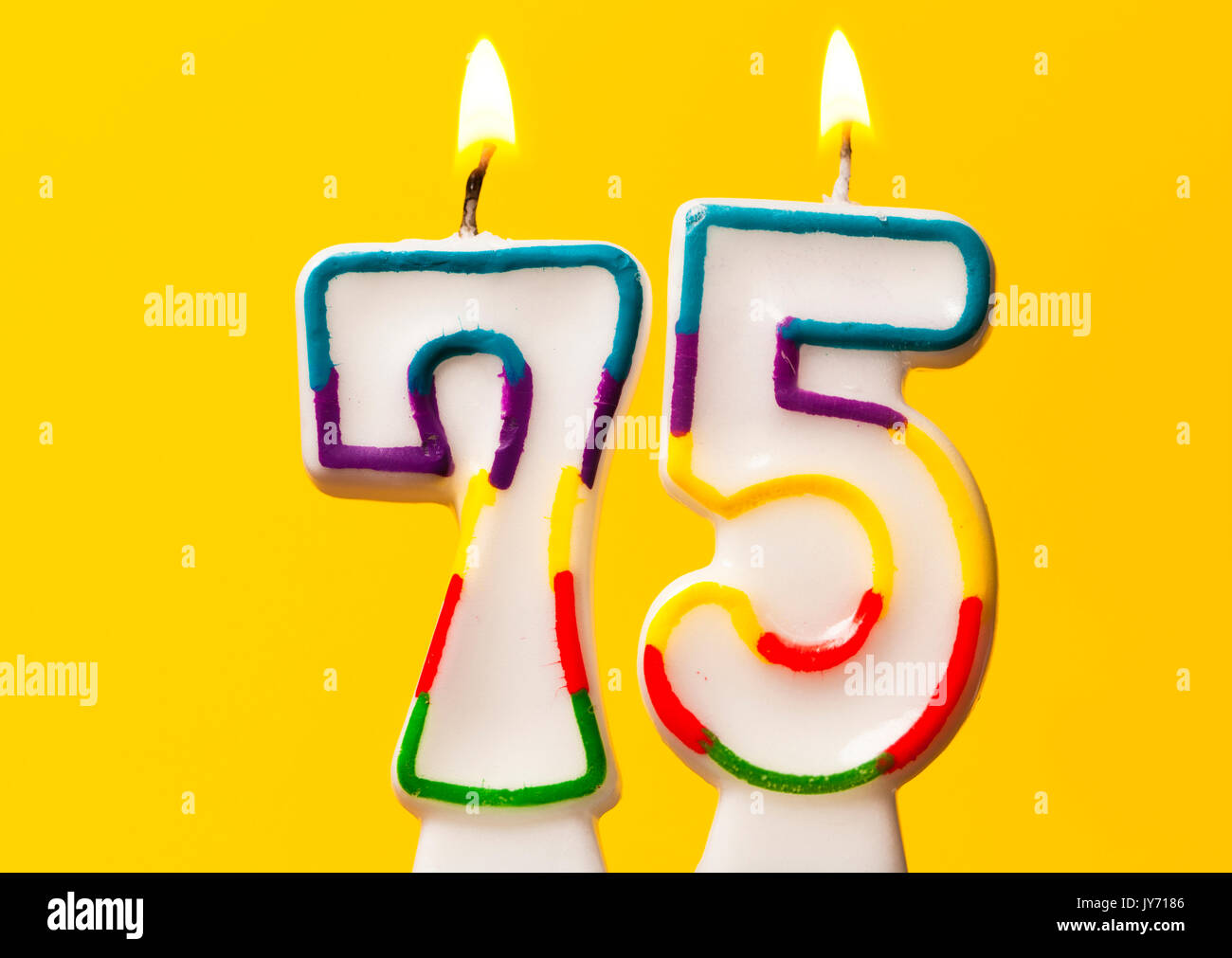 Number 75 birthday celebration candle against a bright yellow ...