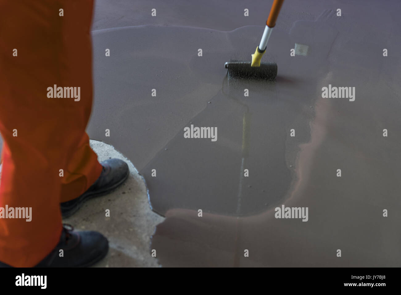 Floor covering with self leveling plaster. Roller application by worker ...