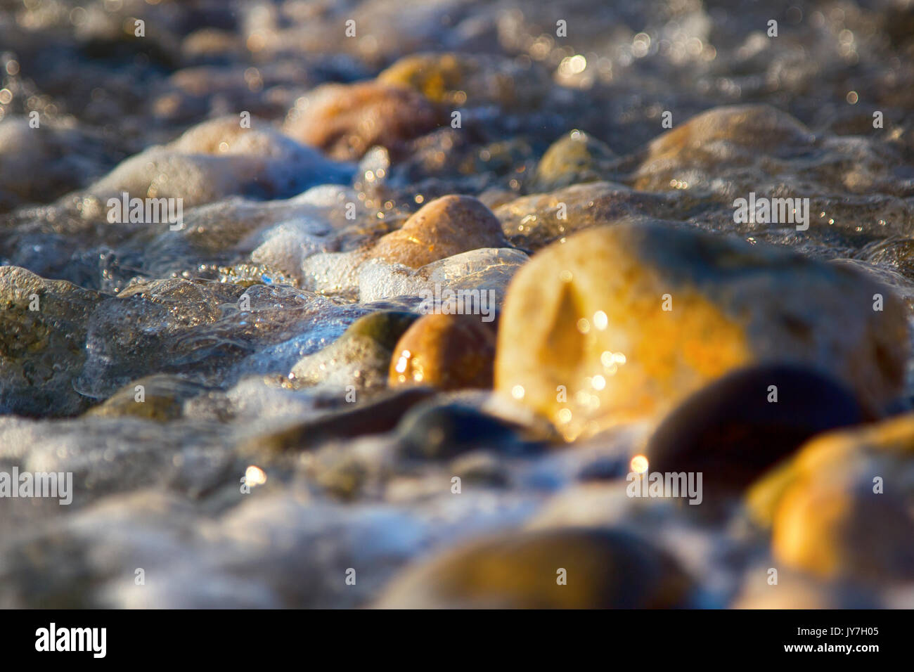 Beach of multi-colored round pebbles, foam and splash of salty waves ...