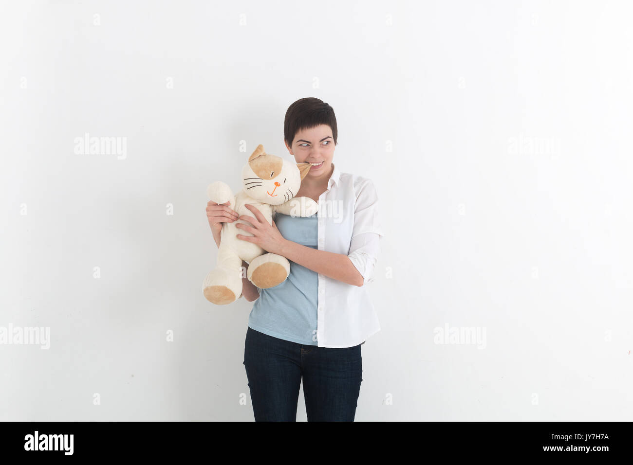 Frustrated attractive young woman biting a plush toy or teddy bear with ...