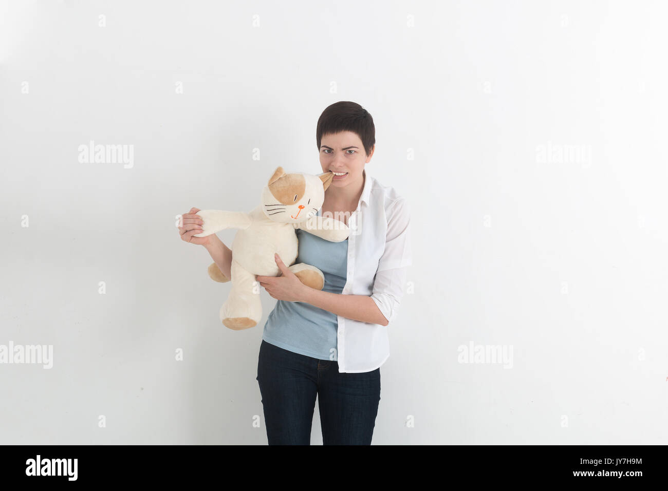 Frustrated attractive young woman biting a plush toy or teddy bear with ...