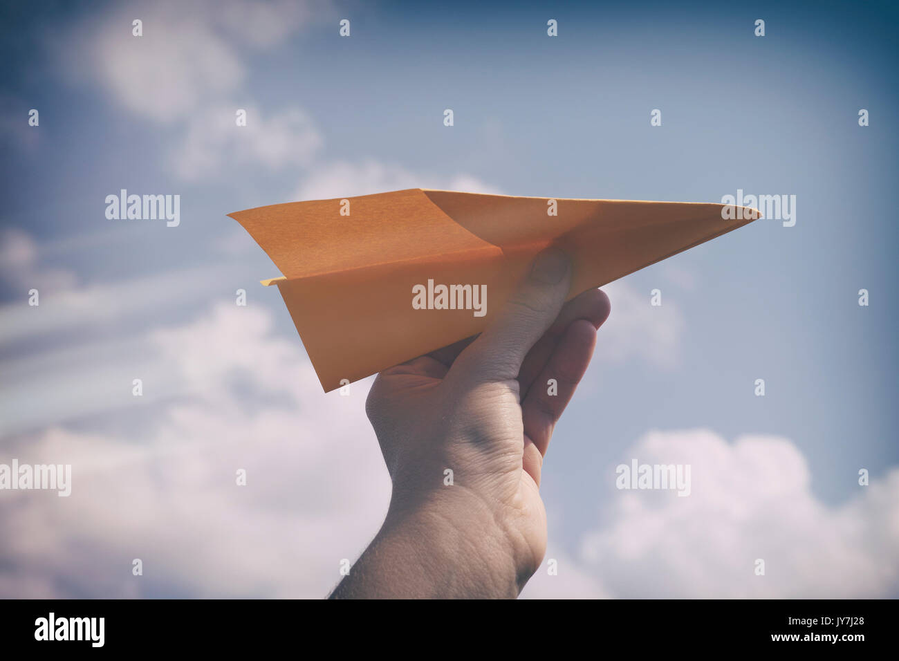 Paper plane in a hand against cloudy sky. Vignette Stock Photo - Alamy