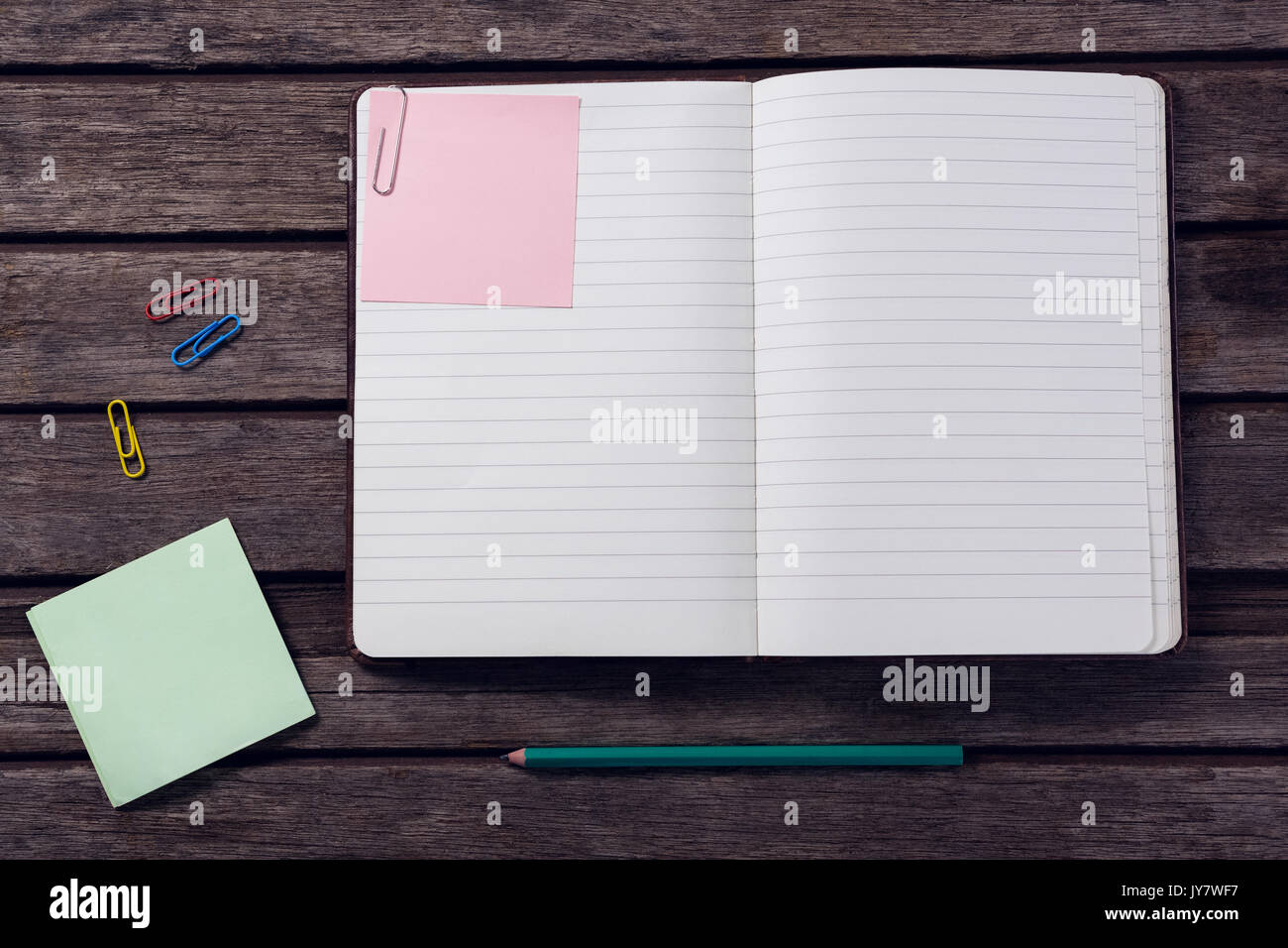 Overhead of diary, sticky notes, pencil and paper clip on wooden table ...