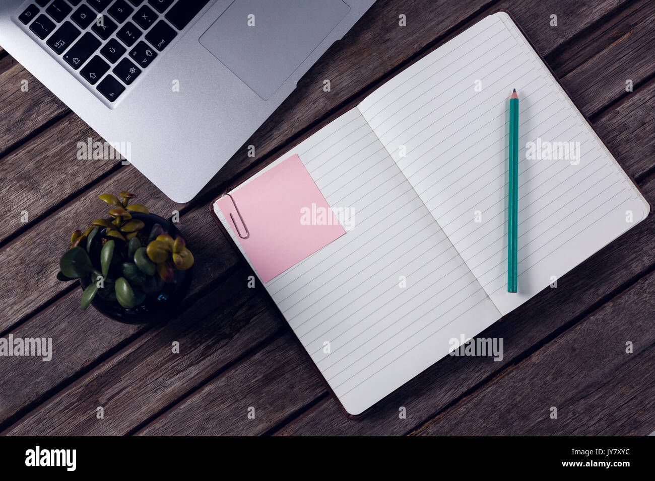 Overhead of laptop, diary, pot plant and cup of coffee on wooden table ...