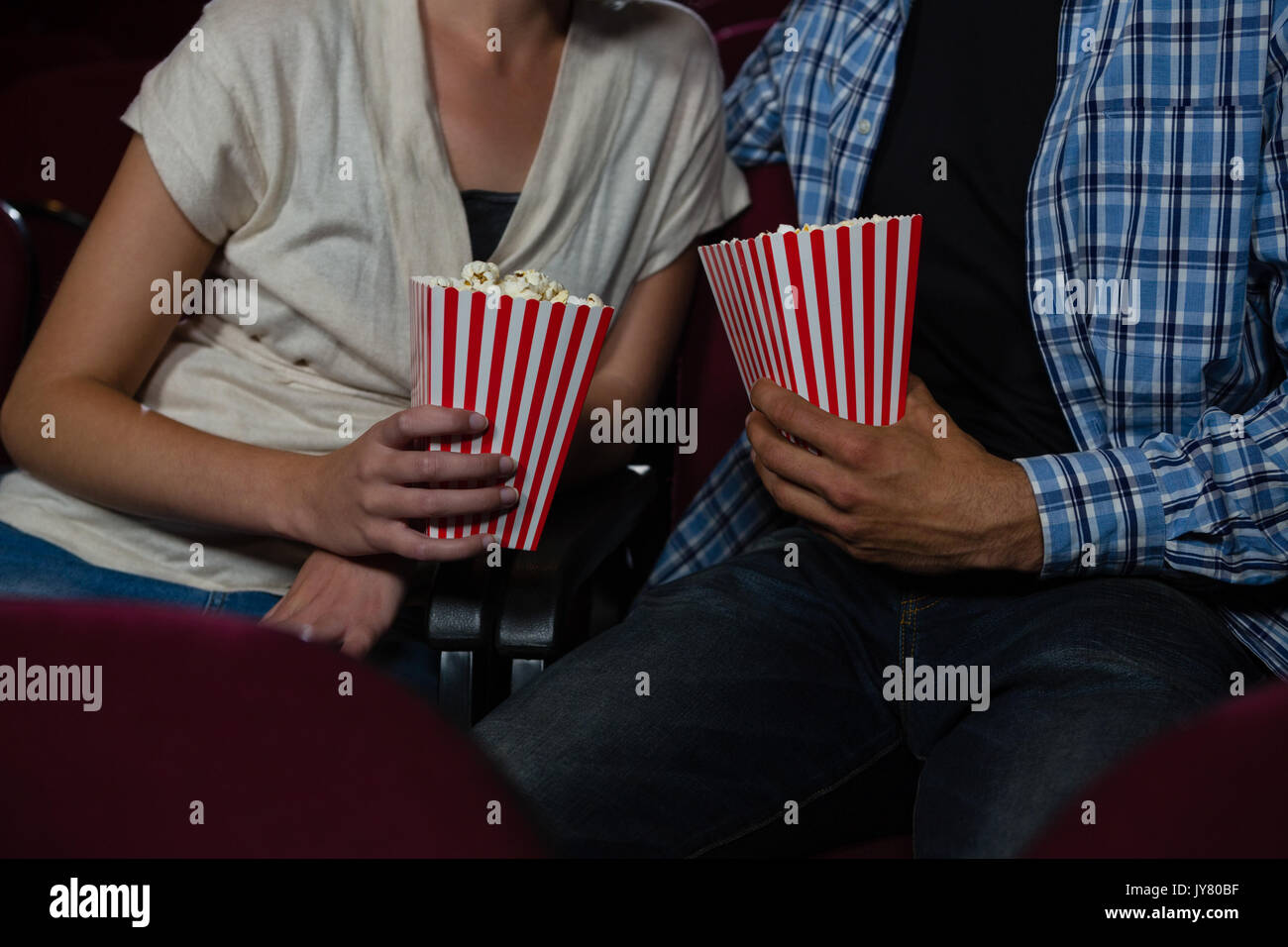 Mid section of couple having popcorn while watching movie in theatre ...