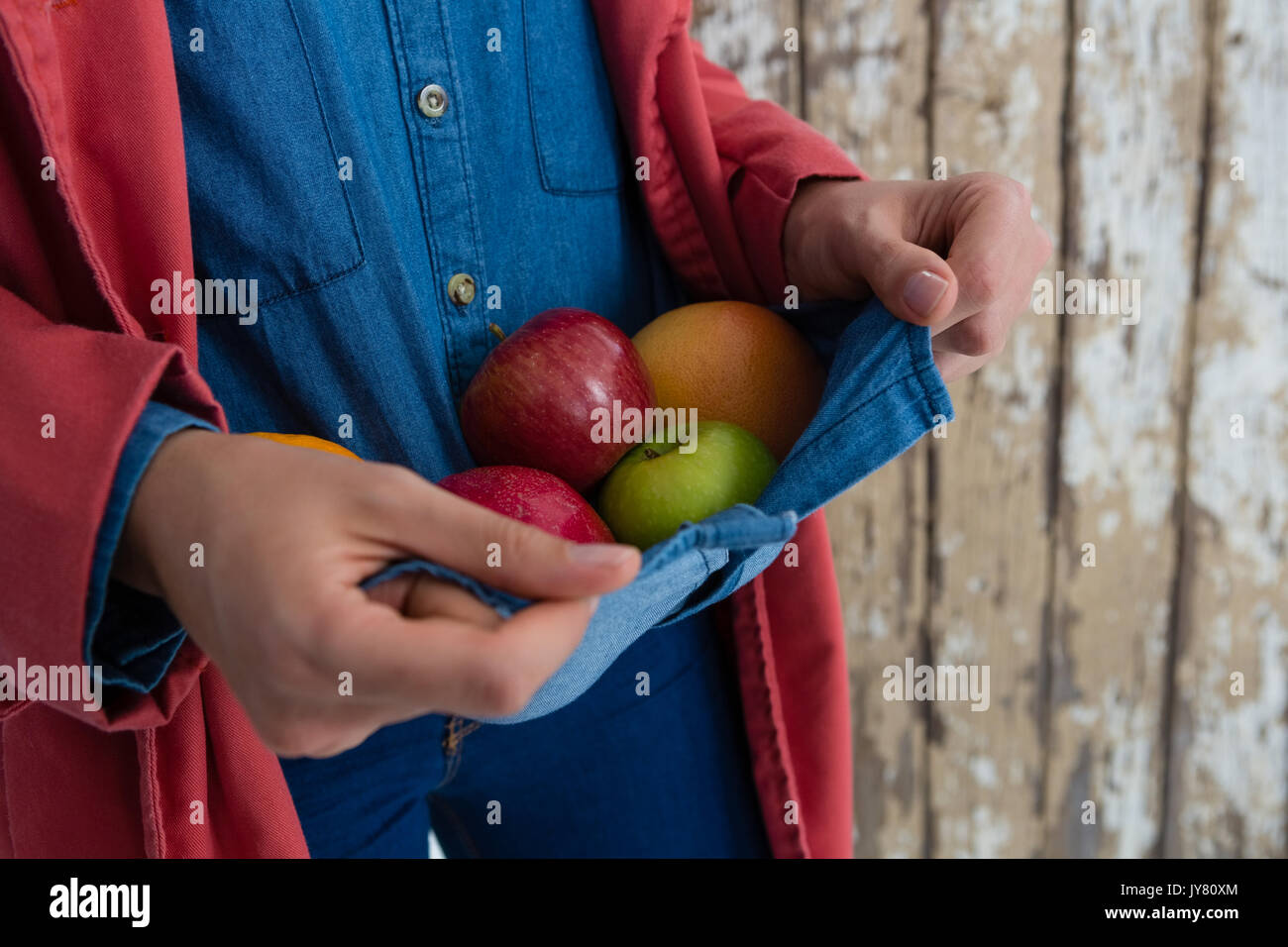 Mid section of woman carrying fruits carrying in shirt while standing ...