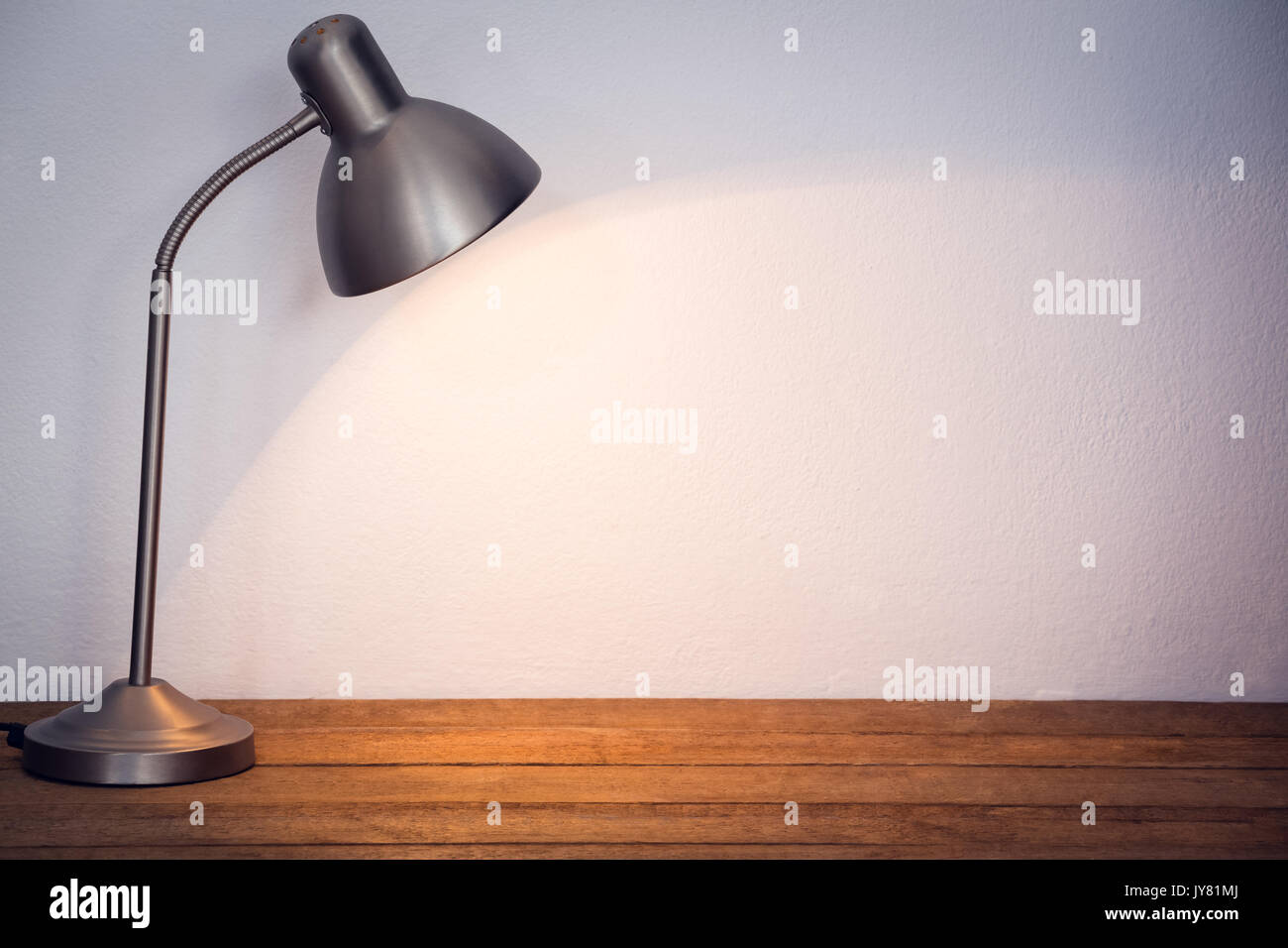 Illuminated table lamp on wooden table by wall in office Stock Photo ...