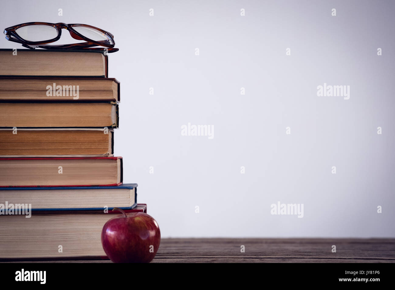 Apple by stack of book with eyeglass at table against wall Stock Photo ...