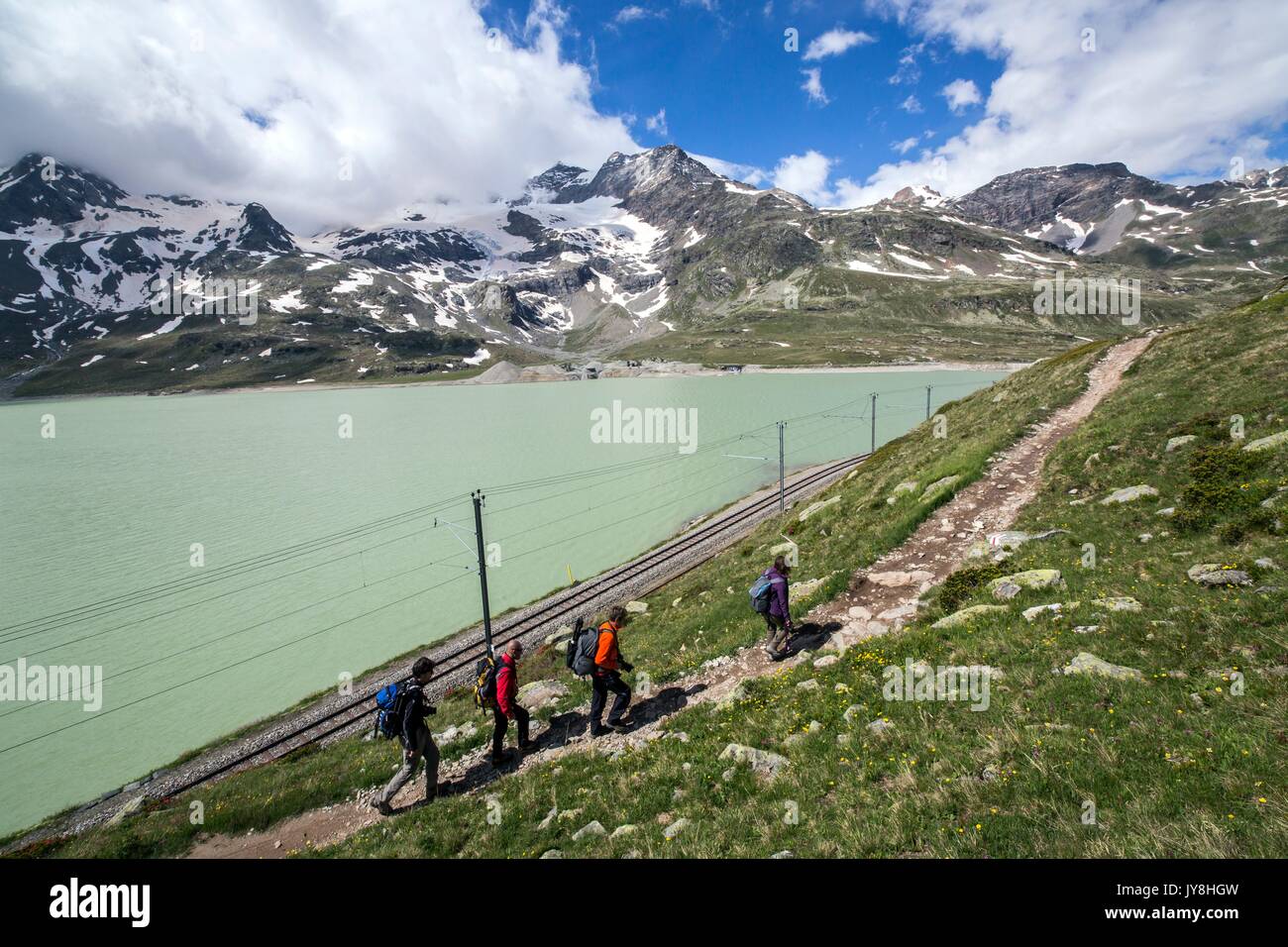 Hikers Walking On The Path That Walks Through The White Lake At Bernina Pass Where Travels The