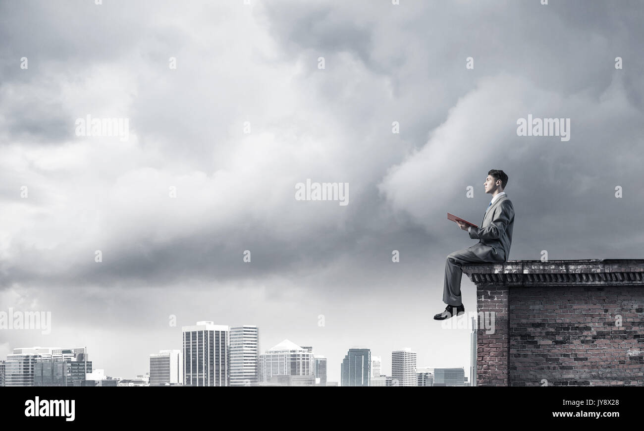 Man on roof edge reading book and cityscape at background Stock Photo ...