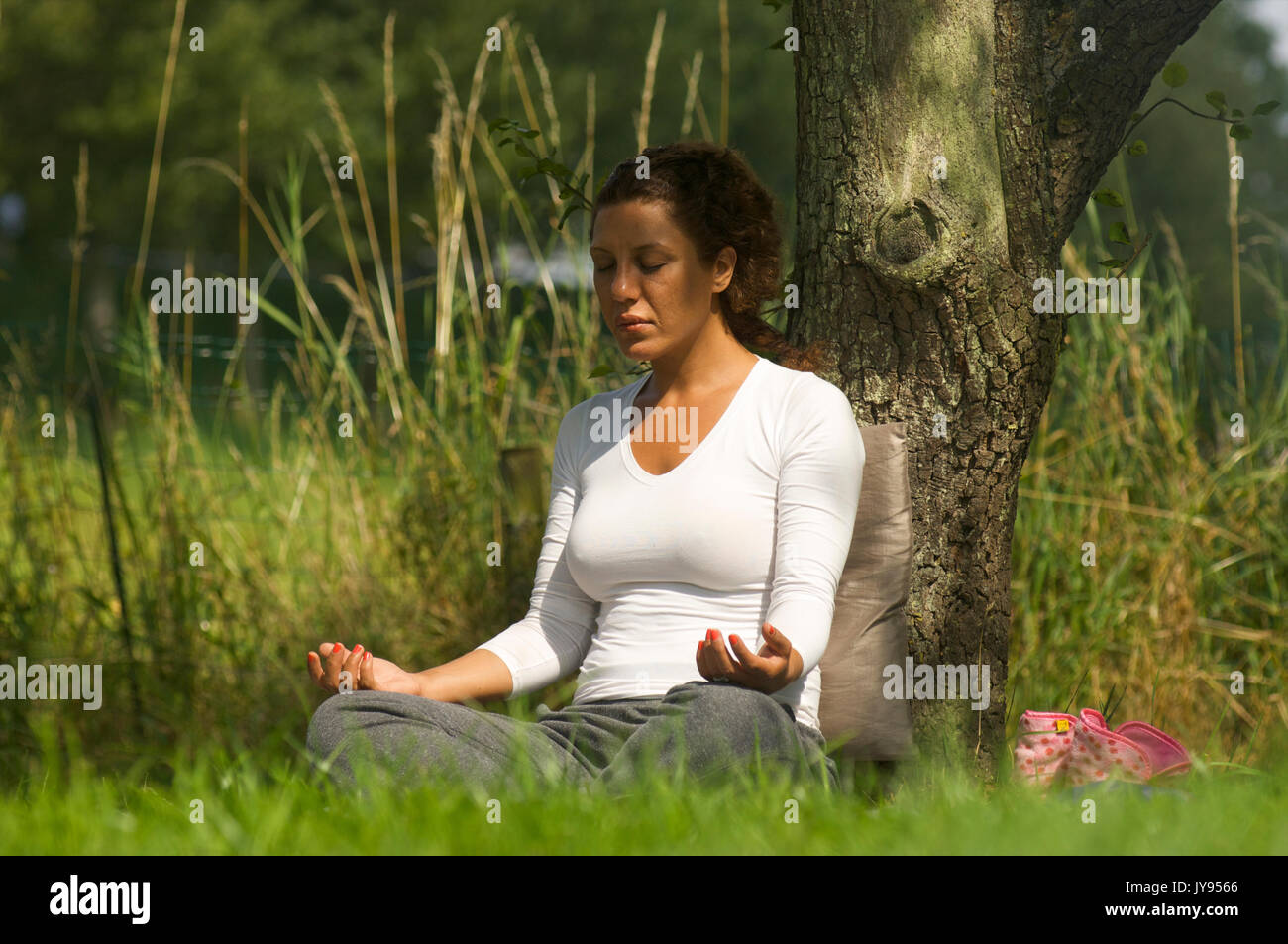 Woman doing a meditation in nature while leaning against a tree Stock ...